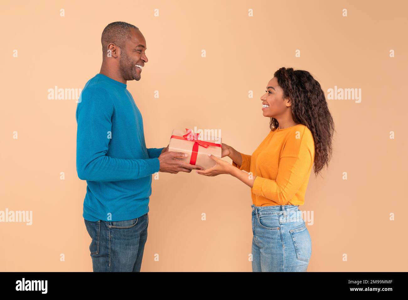 Excitede black couple giving gifts to each other, peach studio ...