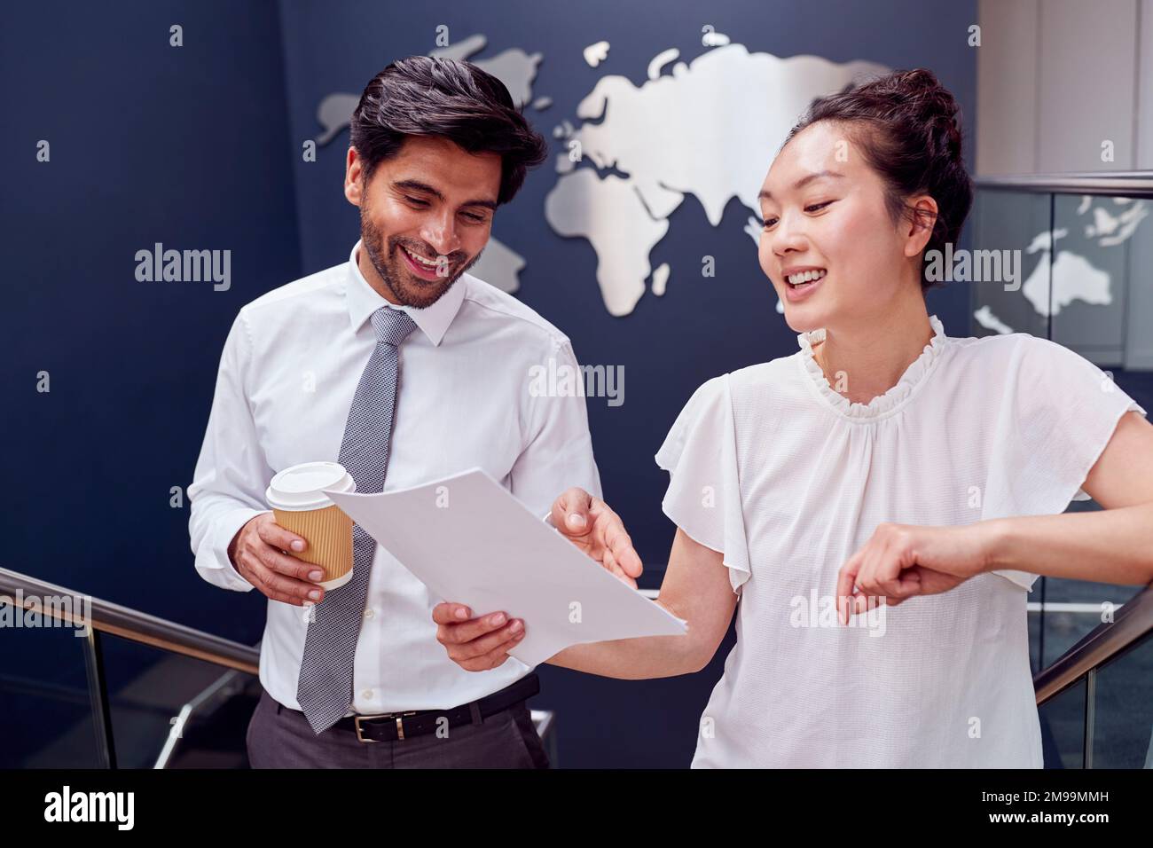 Two Business Colleagues Have Informal Meeting On Stairs Of Office With World Map In Background ...