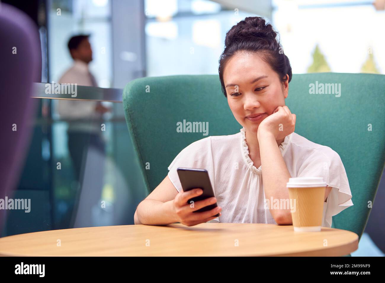 Businesswoman With Mobile Phone Working At Table In Breakout Area Of ...