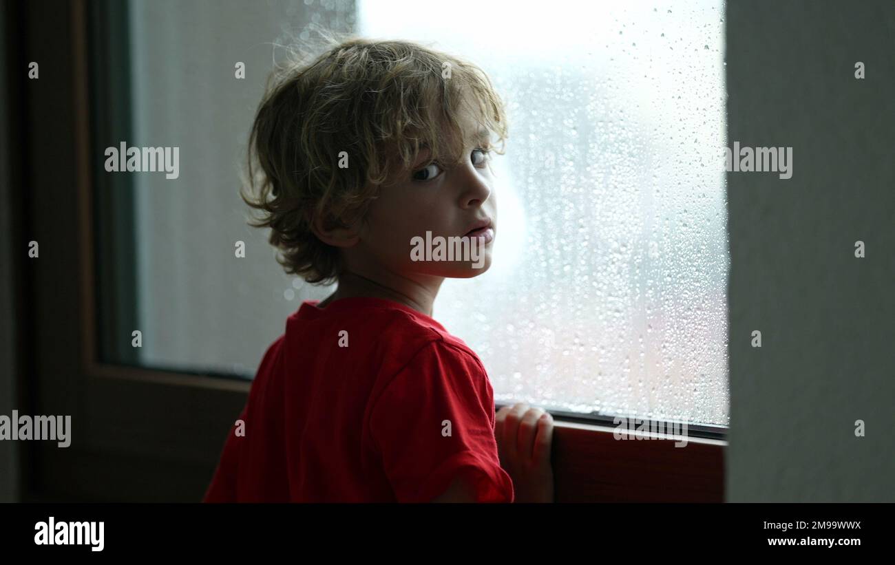 Pensive child looking out window during rainy day. Thoughtful young boy ...