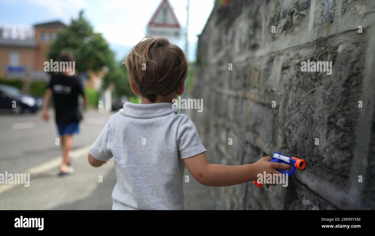 Little boy walking on city sidewalk. Toddler walks outside playing ...