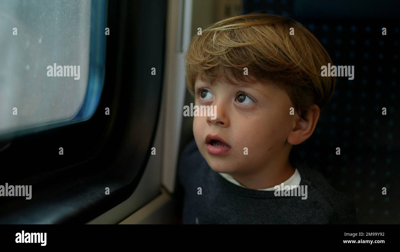 Little boy traveling by train staring outside through train window ...