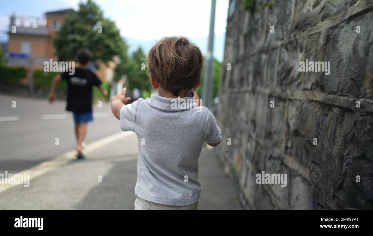 Little boy walking on city sidewalk. Toddler walks outside playing ...