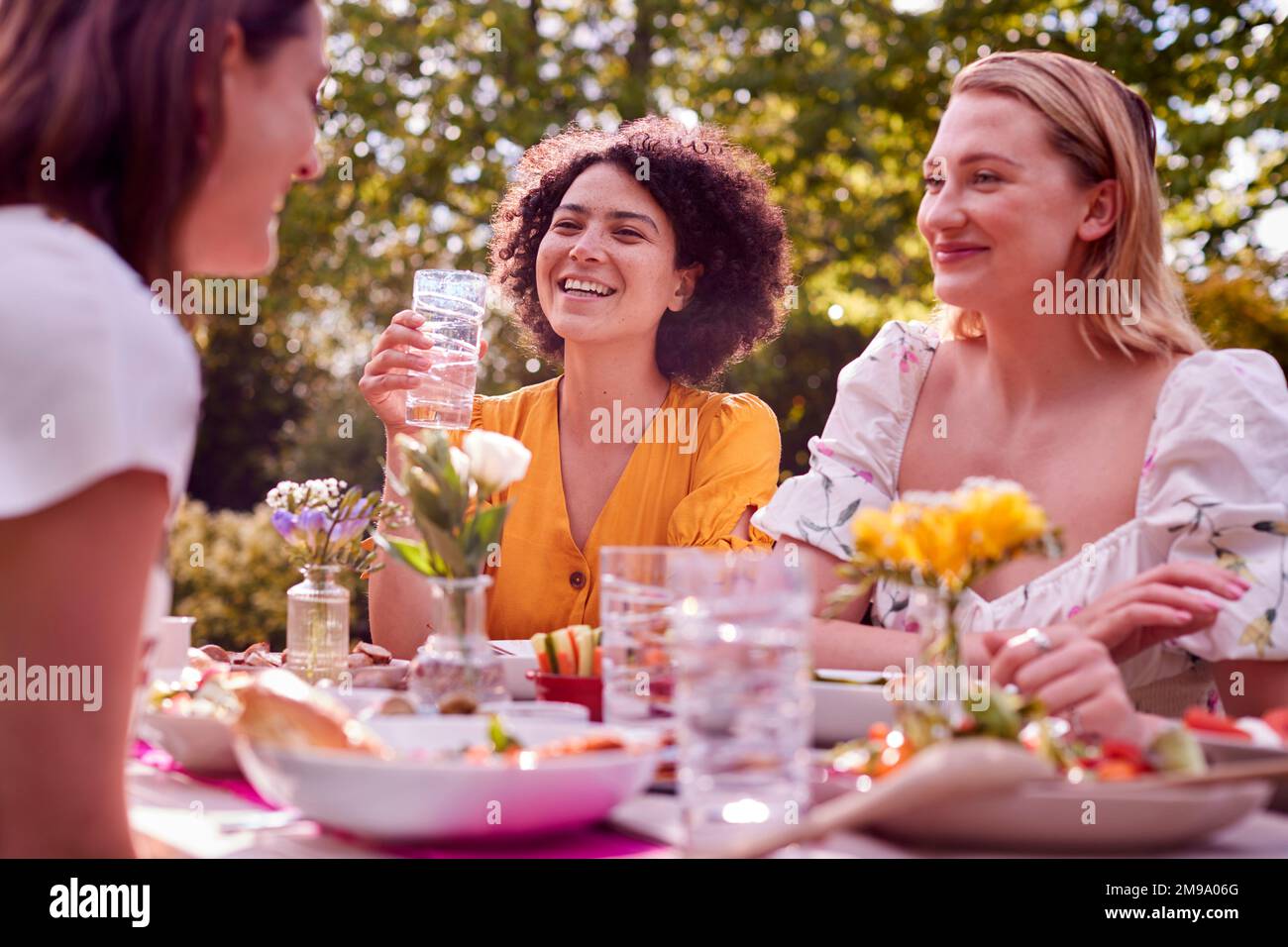 Three Female Friends Sitting Outdoors In Summer Garden At Home Eating ...