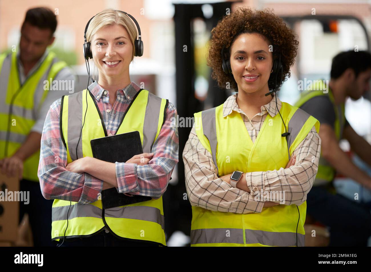 Portrait Of Two Female Workers Using Headsets In Distribution Warehouse ...