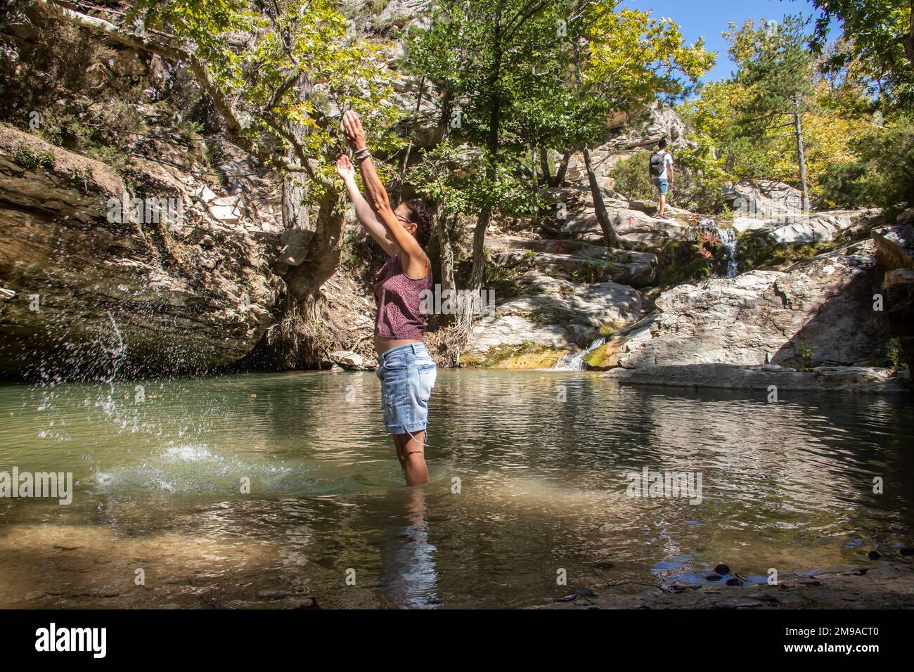 Young woman splashing clean pure water from forest lake around her ...