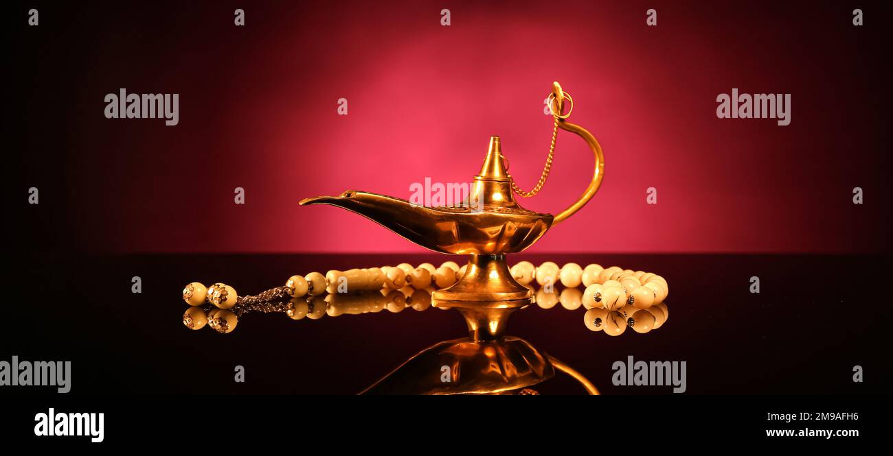 Aladdin lamp of wishes and prayer beads on table against dark red ...
