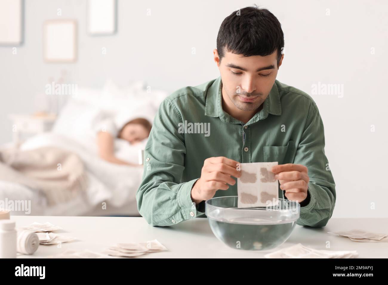 Young man dipping mustard plaster into bowl of water in bedroom Stock ...