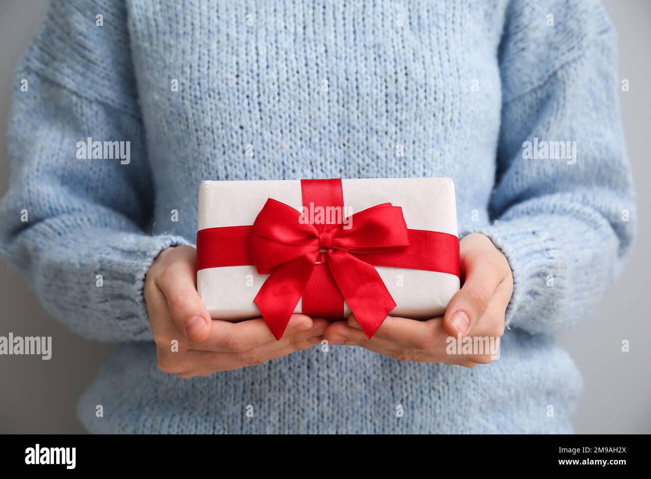 Woman in blue sweater with gift box for Valentine's Day on grey ...