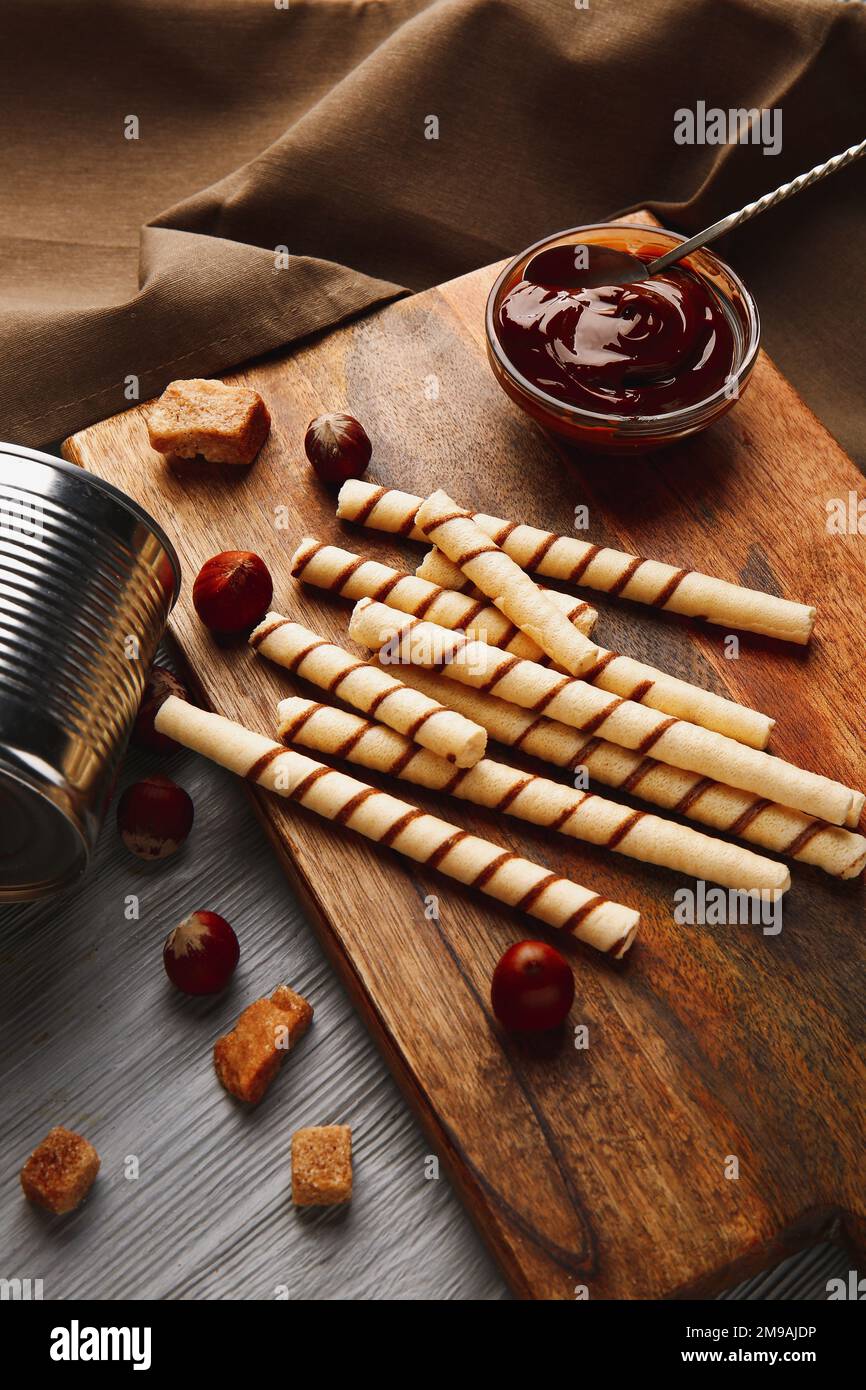 Wooden board with tasty wafer rolls, nuts, tin can and bowl of boiled ...