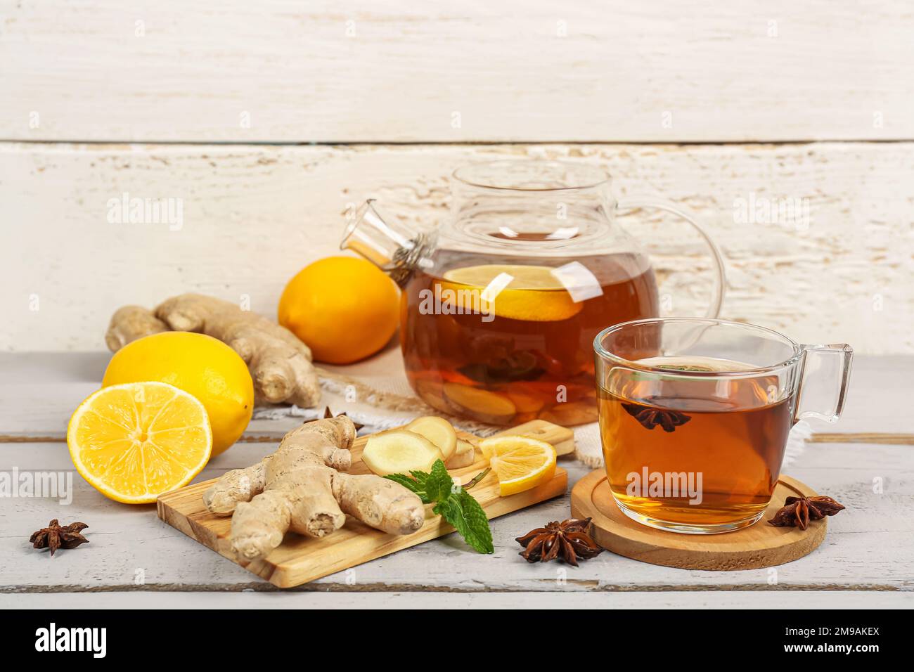 Ginger root, glass cup of black tea, teapot, and lemon on wooden table ...