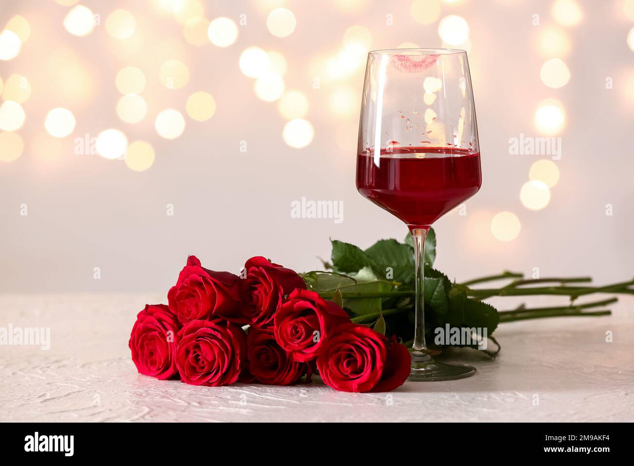 Glass of wine and beautiful rose flowers on white table against blurred ...