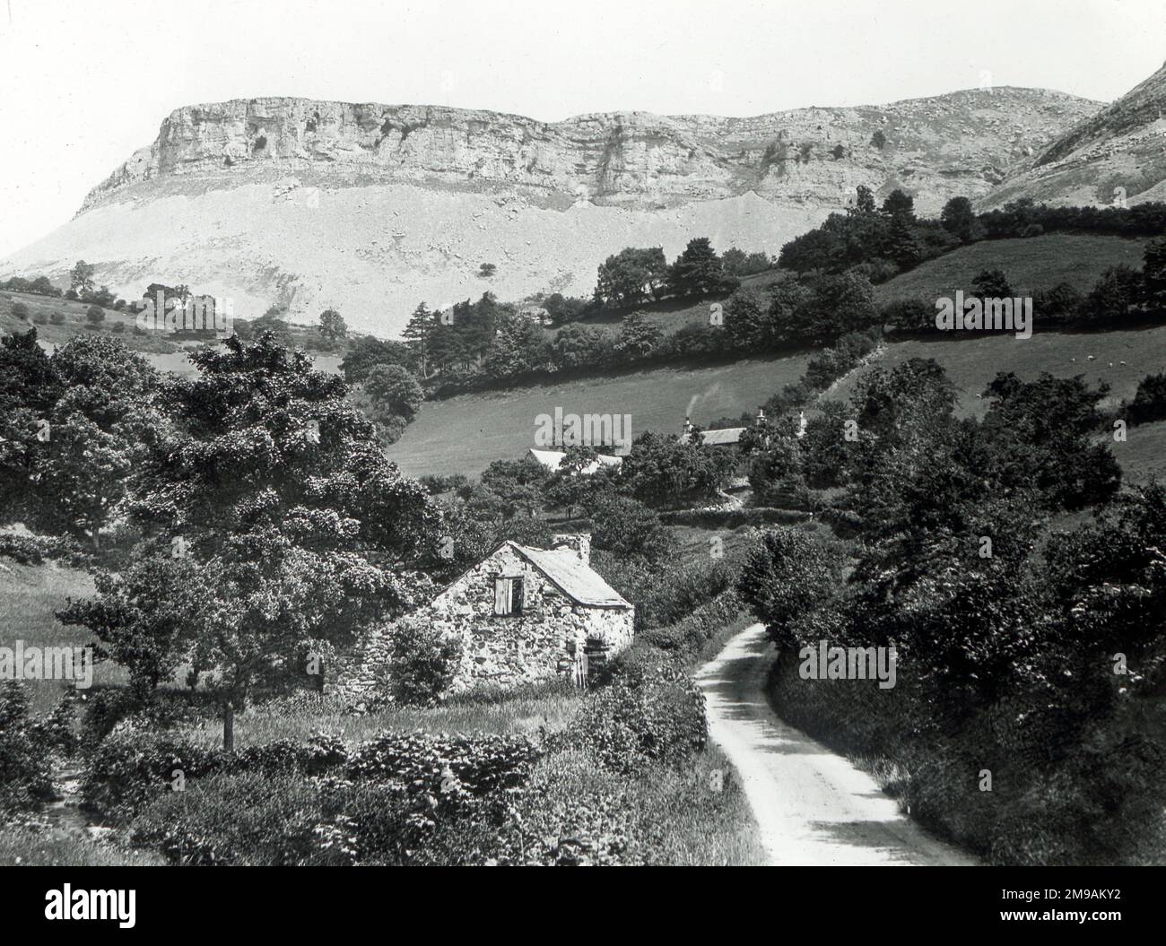 Quiet Welsh country lane with steep rocky escarpment looming in the ...