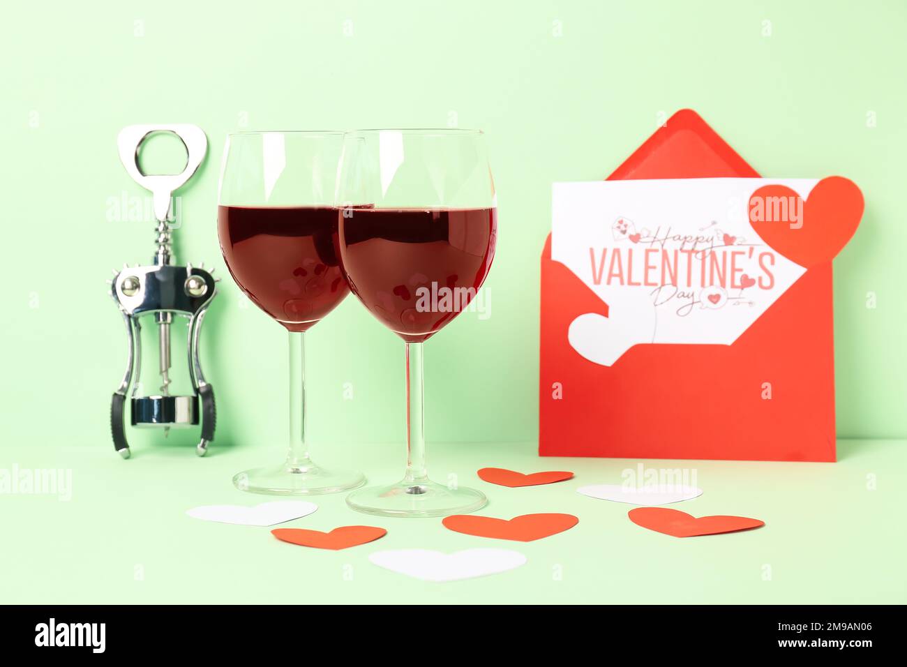 Glasses of wine, envelope with greeting card and opener on green ...