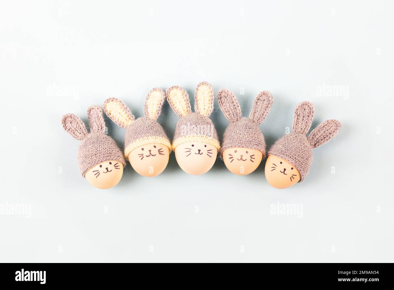 Five Easter eggs with funny faces and gray crocheted hats with bunny ...