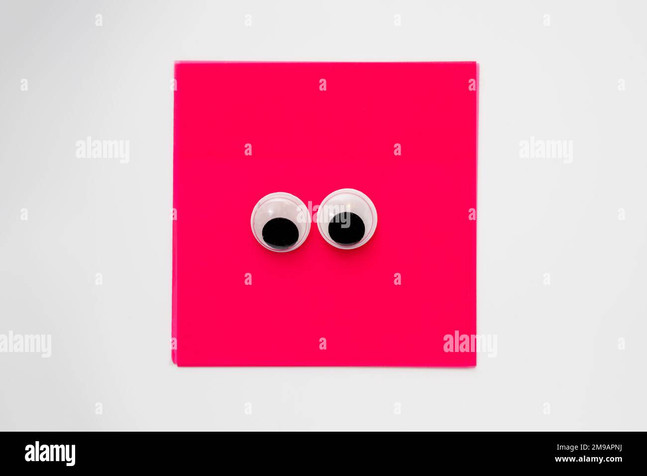 Pair of cute googly eyes on pink square note pad isolated on a white ...