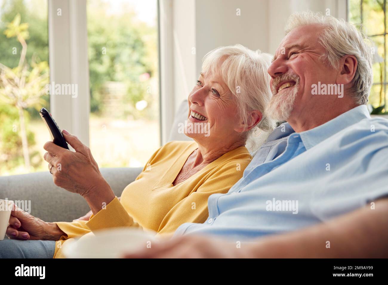 Retired Senior Couple Sitting On Sofa At Home With Remote Control ...