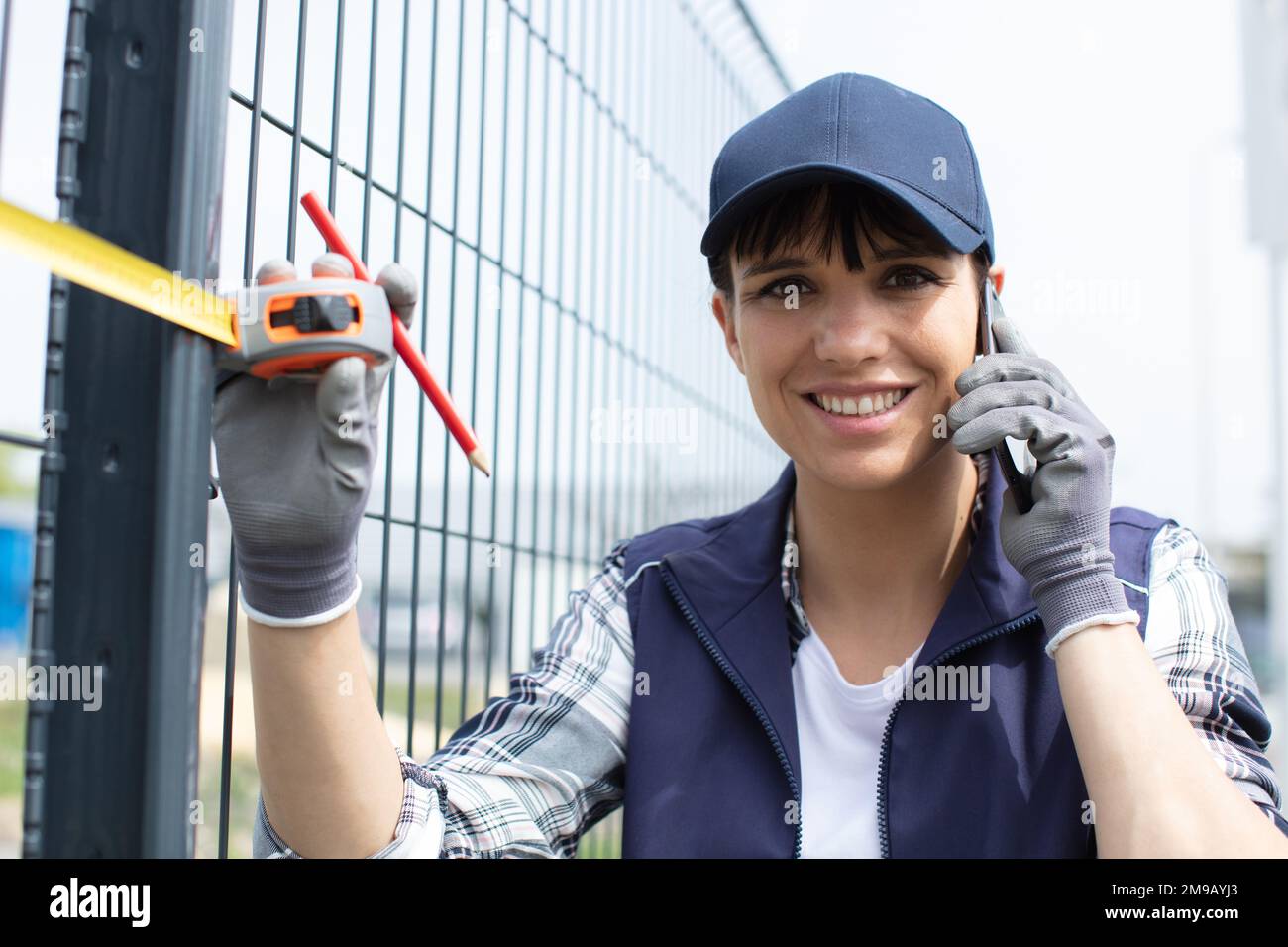 worker woman measuring metal mesh fence while calling Stock Photo - Alamy
