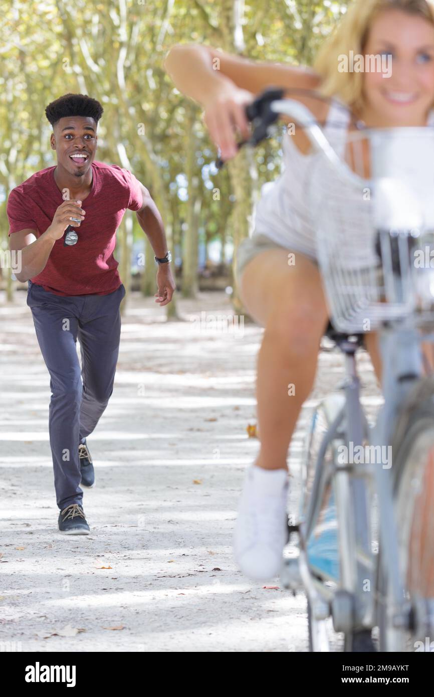 happy couple running behind woman riding bicycle Stock Photo - Alamy
