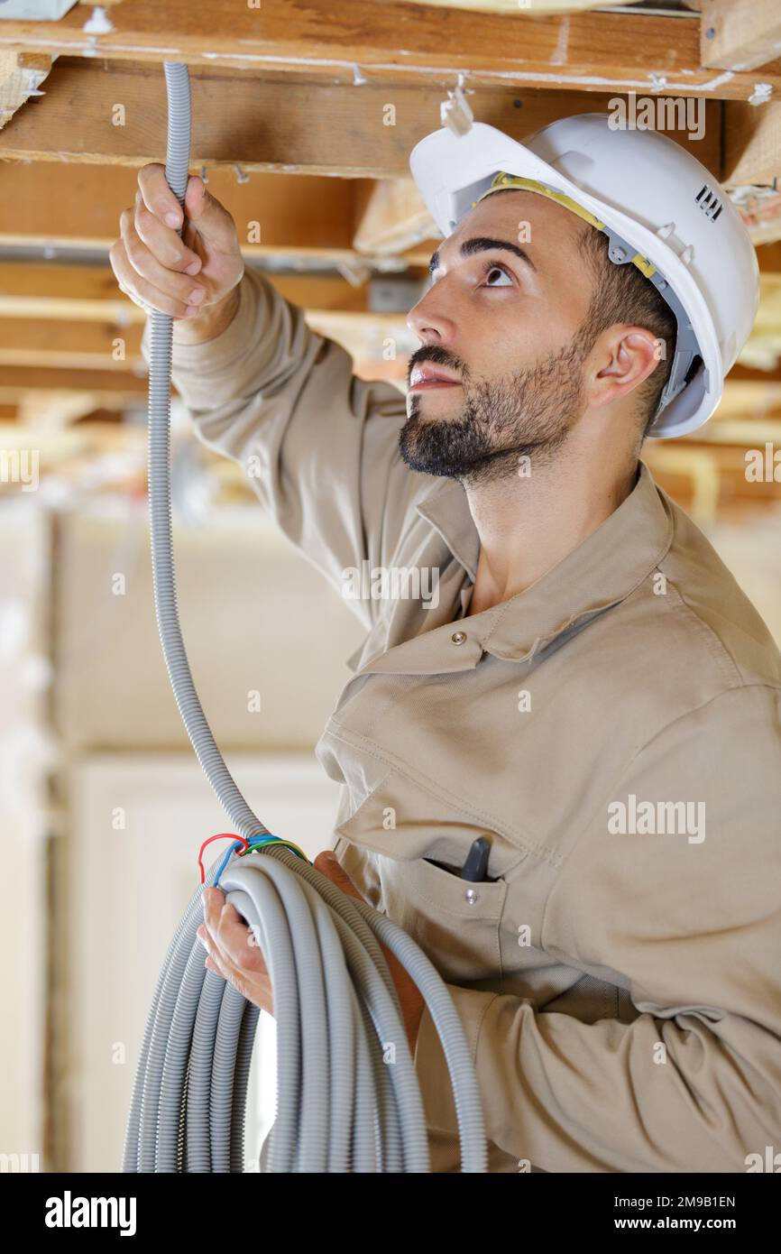 tradesman installing cable ducting into roof space Stock Photo - Alamy
