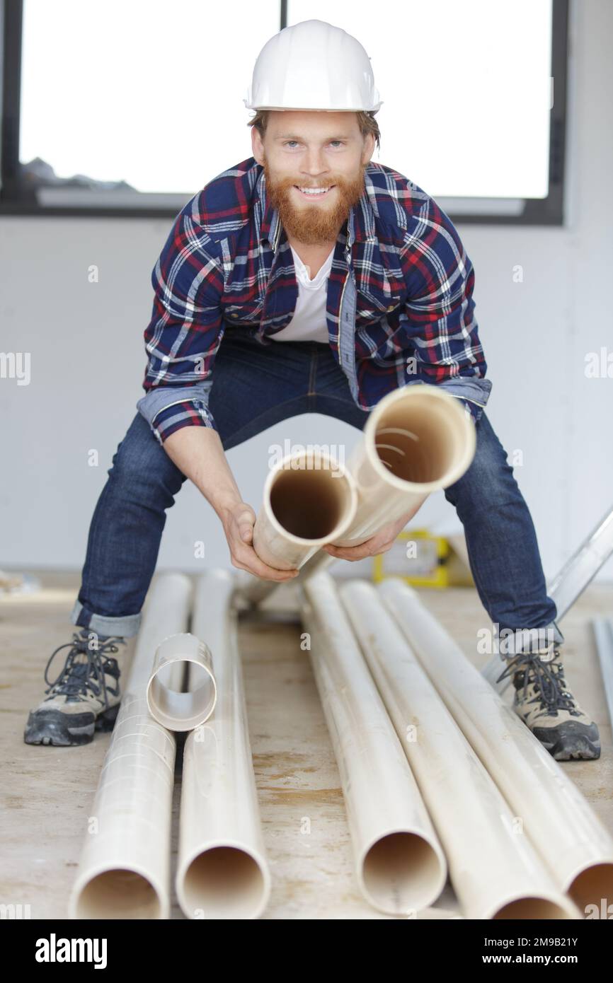 builder standing with ventilation pipe at the construction site indoors ...