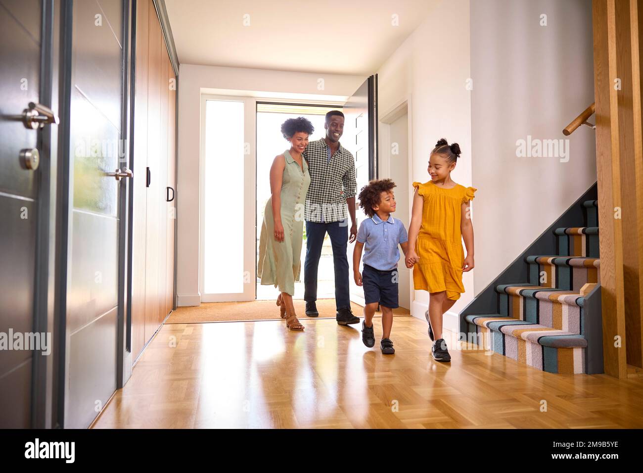 Family Coming Home After Day Out Opening Front Door And Walking Into ...