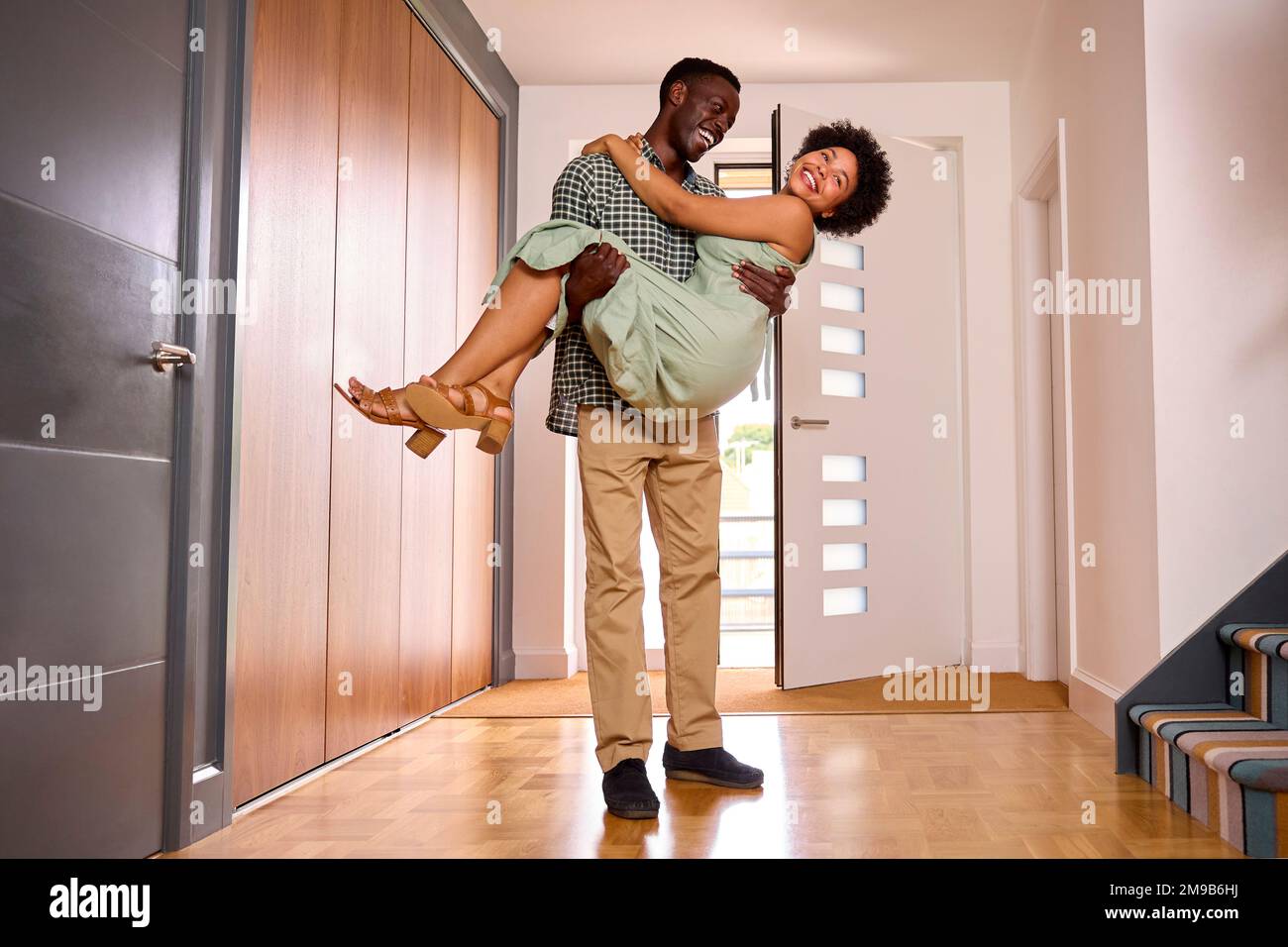 Romantic Couple With Man Carrying Woman Over Threshold Into Hallway Of ...