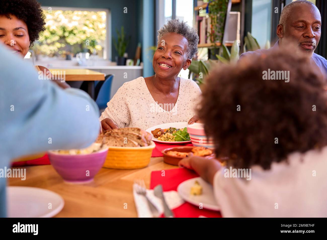 Multi-Generation Family Sitting Around Table At Home Enjoying Meal ...