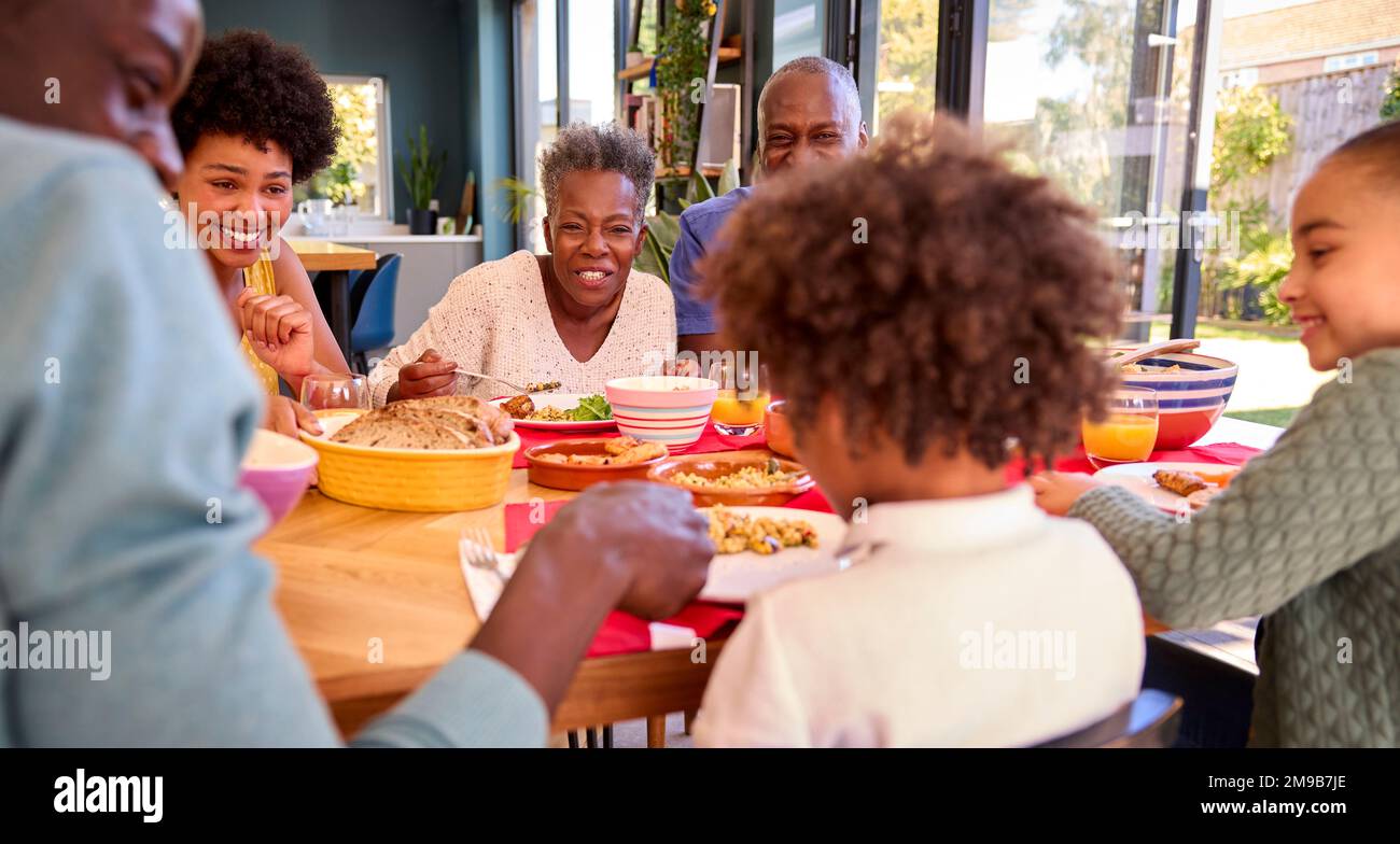 Multi-Generation Family Sitting Around Table At Home Enjoying Meal ...