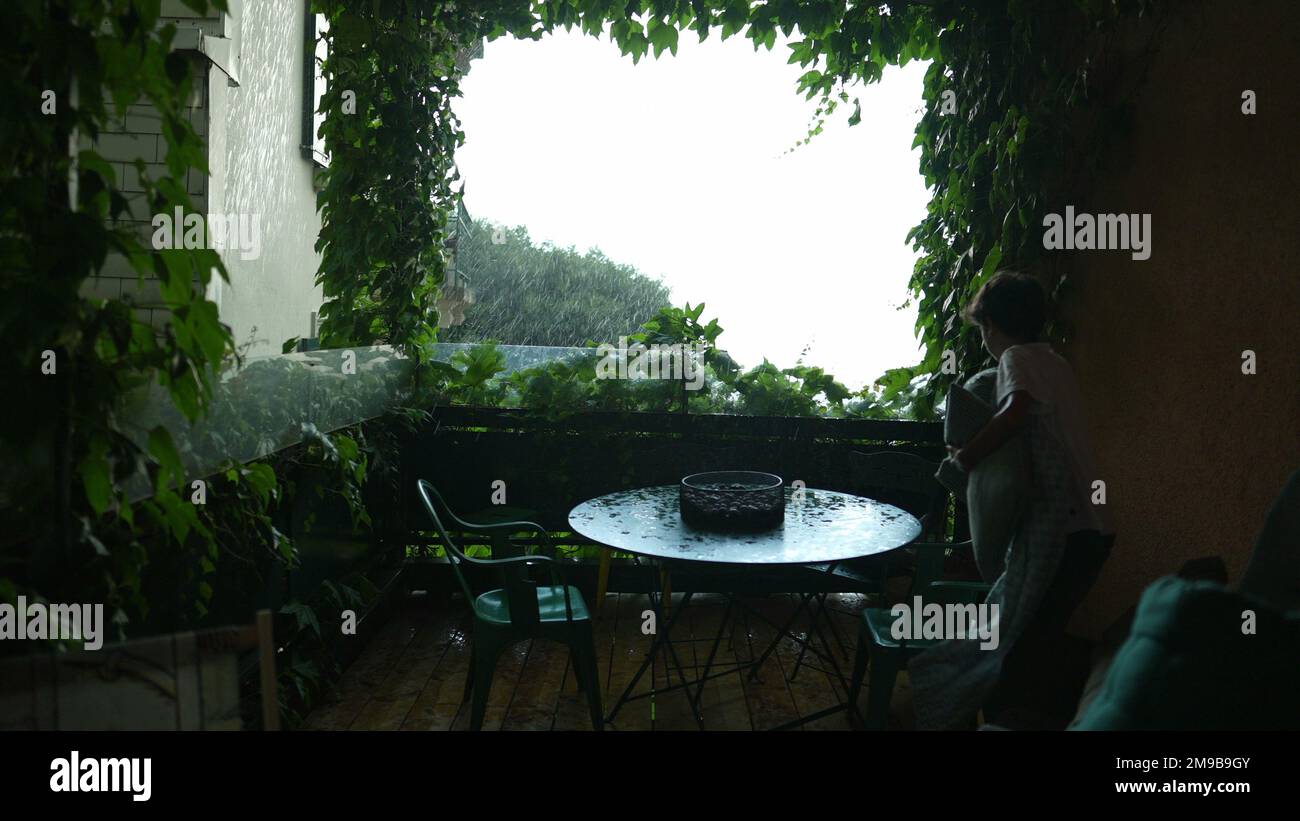 Pouring rain, child removing pillows and clothes from terrace balcony ...