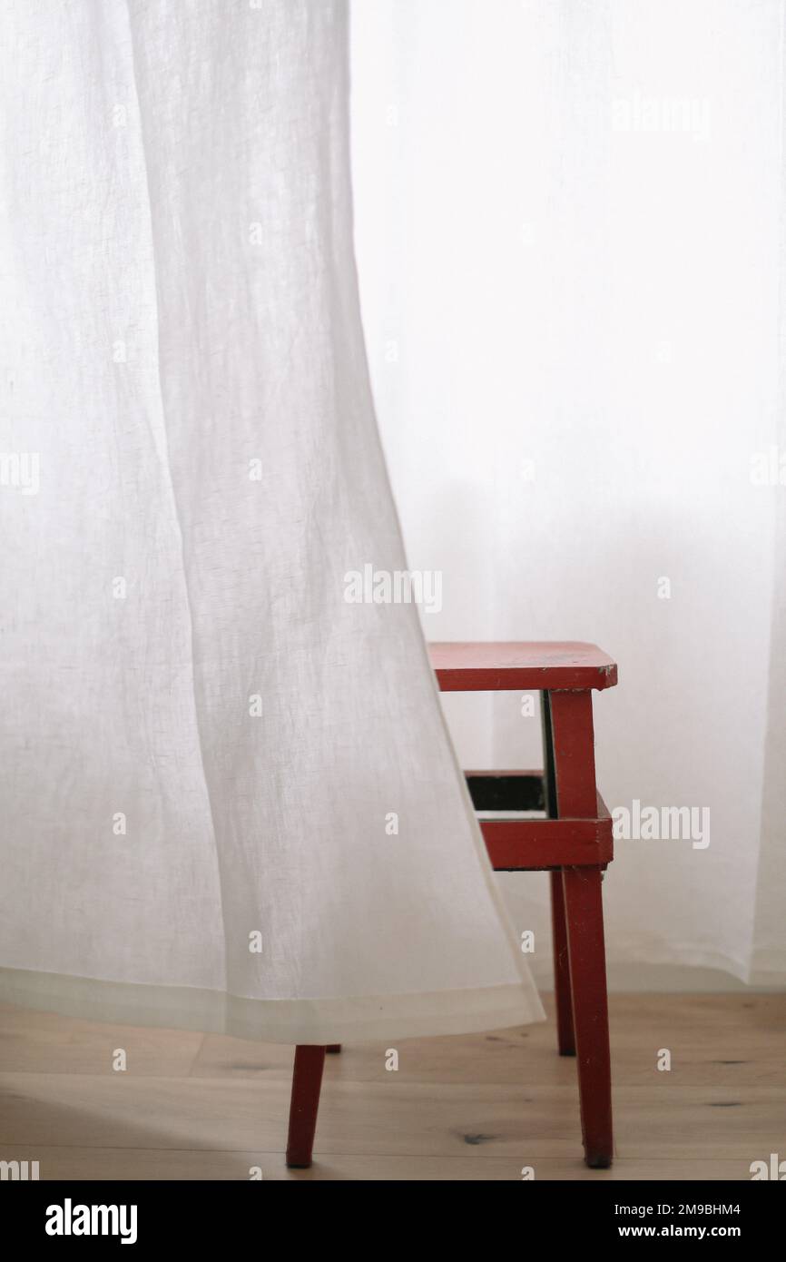 Wooden chair near window with white waving curtains. Room with sunlight ...