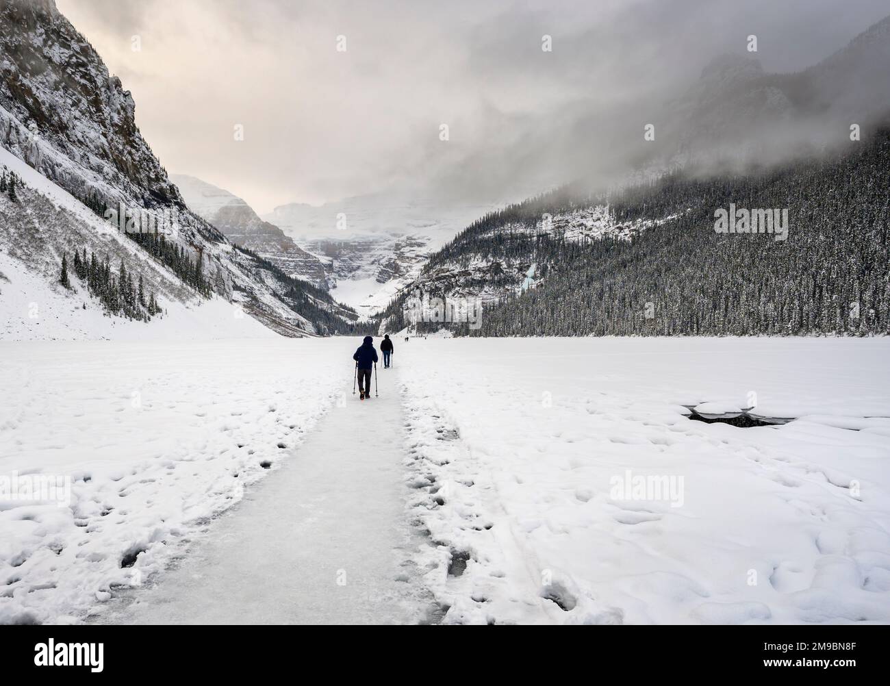 Two unidentifiable people walk across frozen Lake Louise in Banff ...