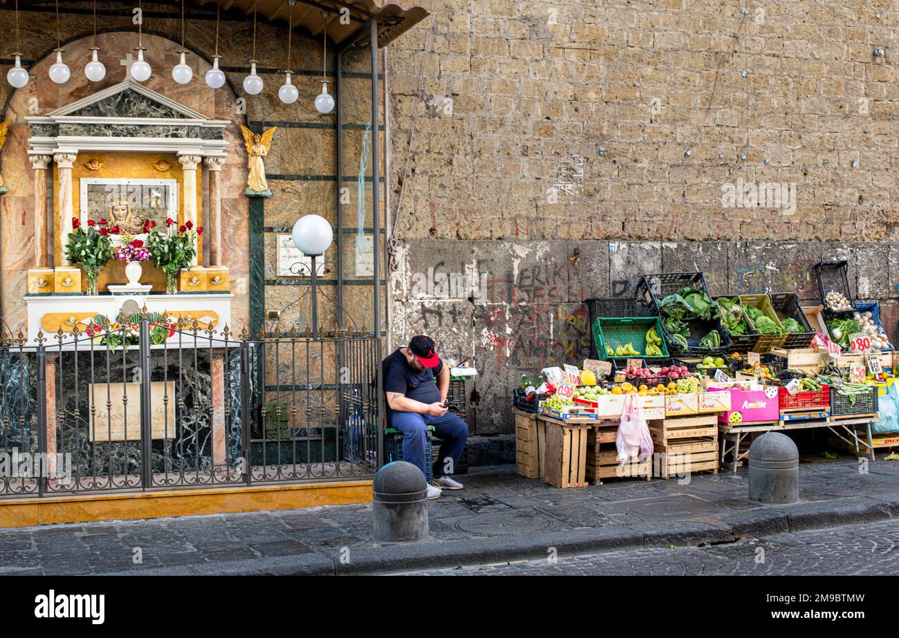 A man sits by his fruit stall beside a grotto under a road bridge in ...