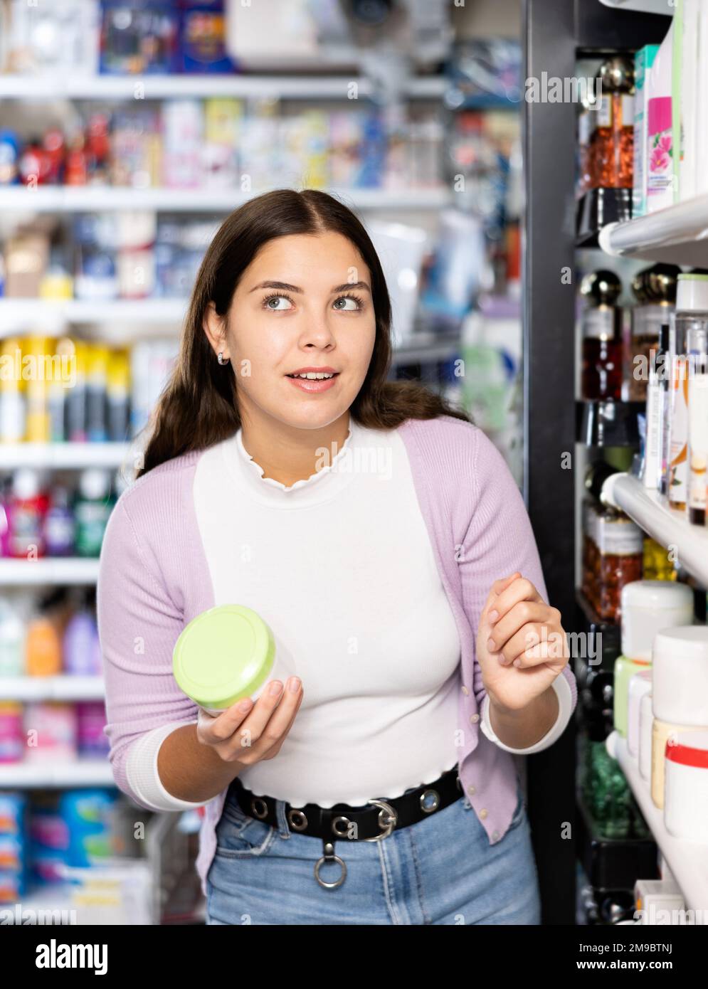 Surprised woman choosing hair care products at cosmetics store Stock ...