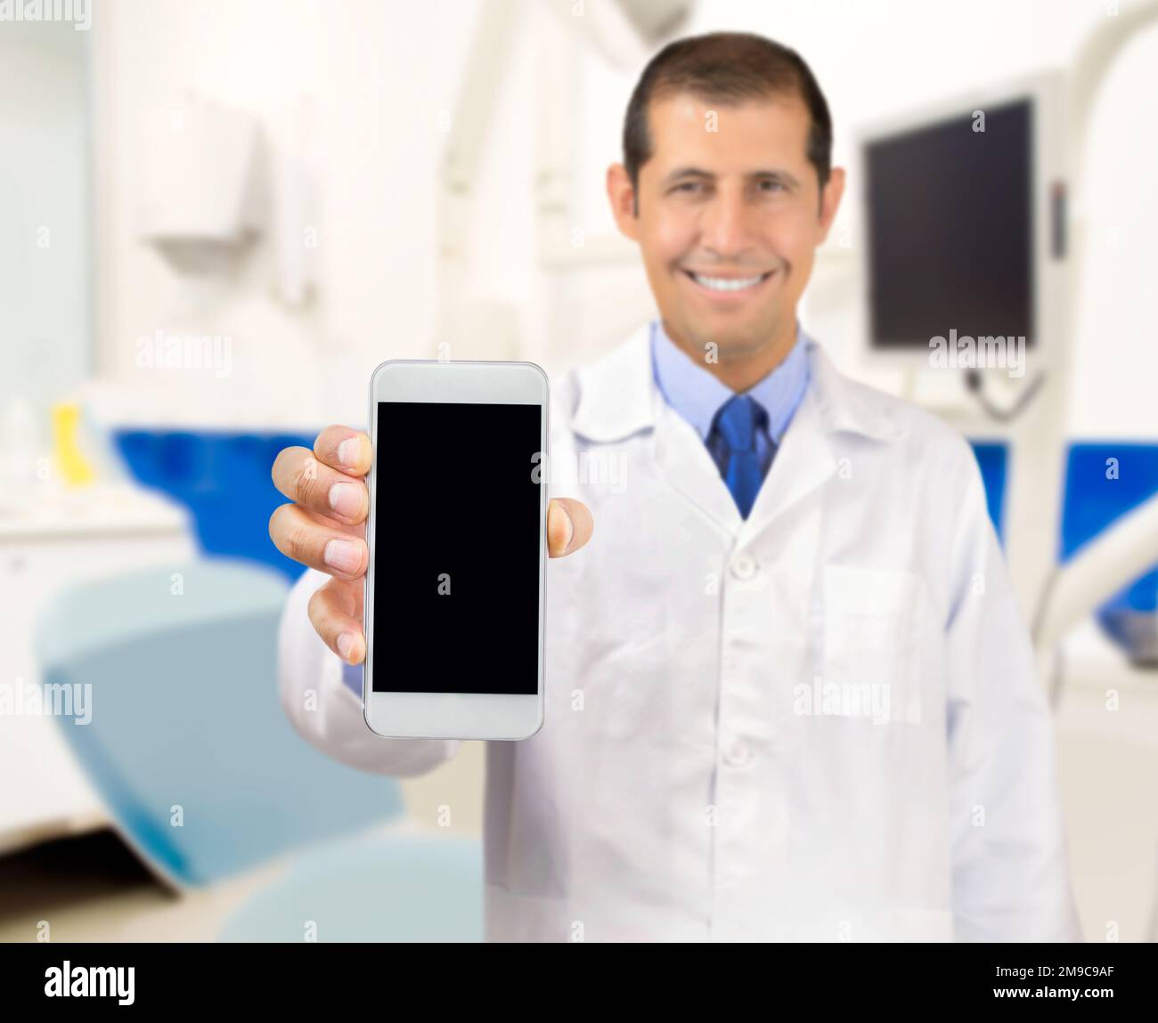 A male dentist standing showing the copy space in a mobile phone at ...