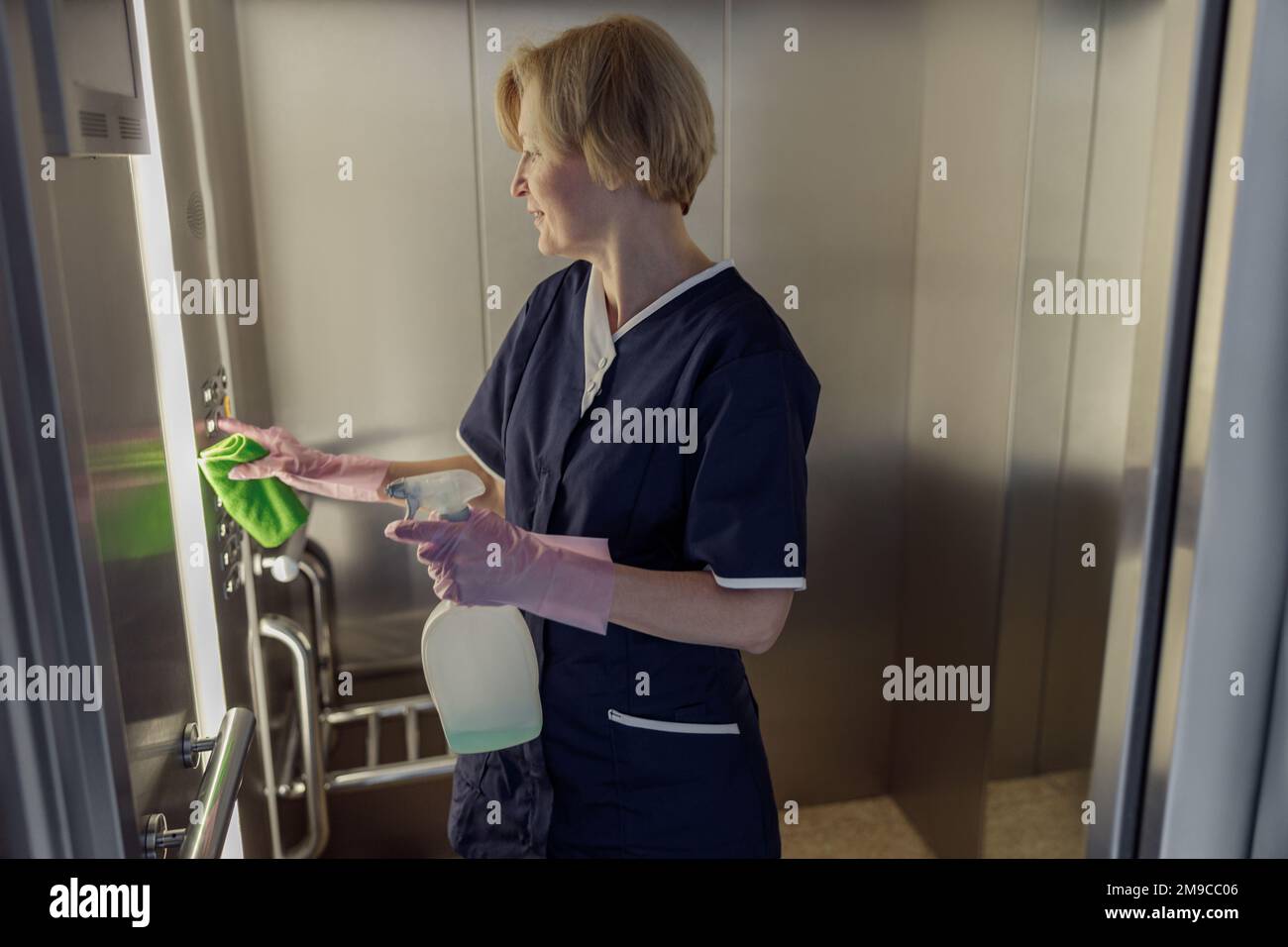 Professional chambermaid wearing uniform and gloves cleaning elevator ...