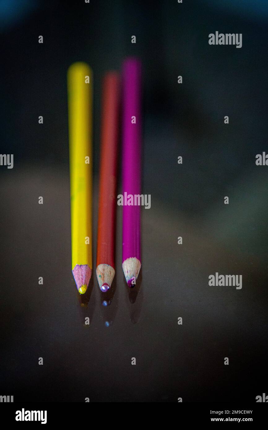 Three colour pencils pointing forward on a reflective surface Stock ...