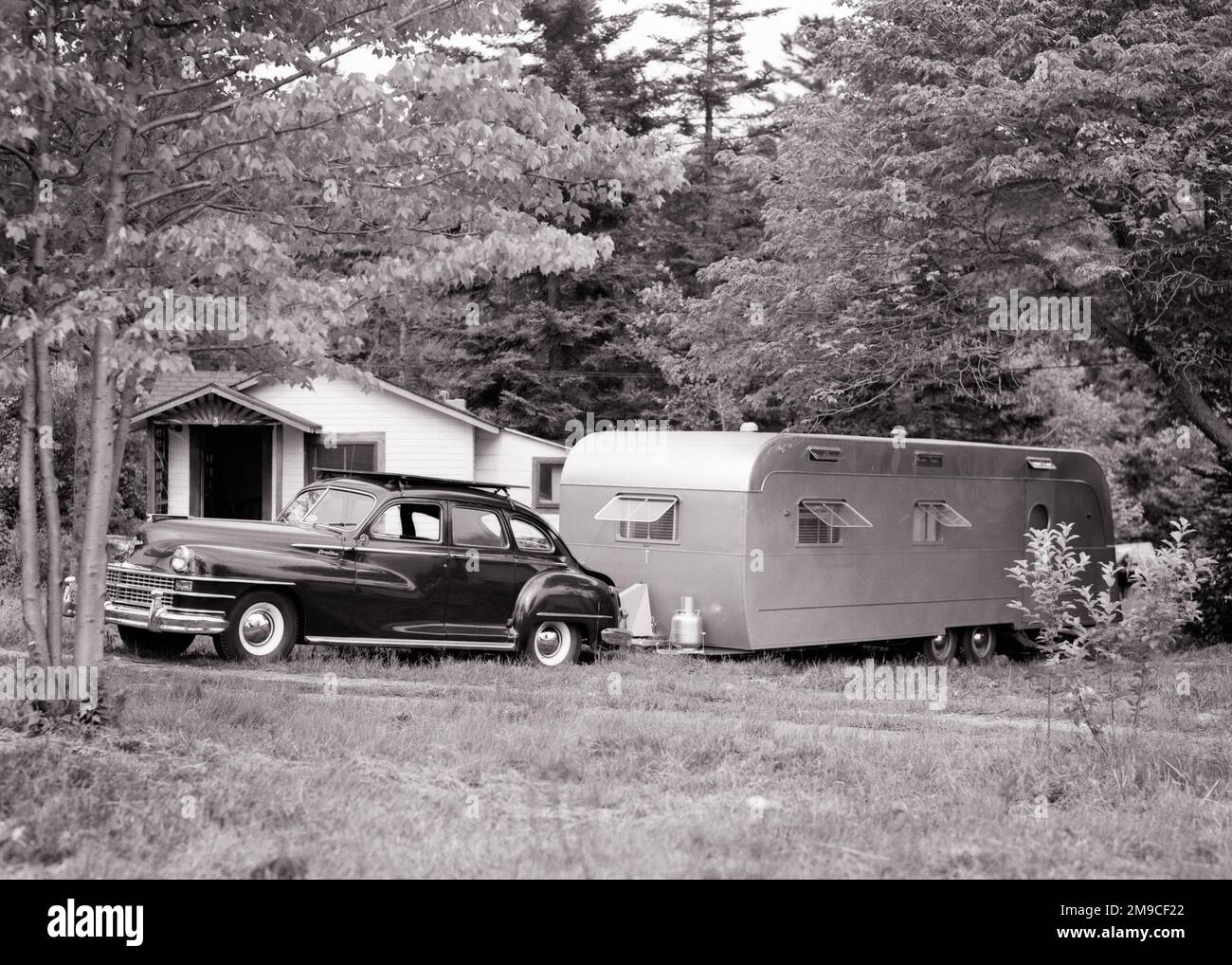 1950s CAR ATTACHED TO RV TRAILER PARKED IN WOODED AREA BY CABIN - m2266 ...