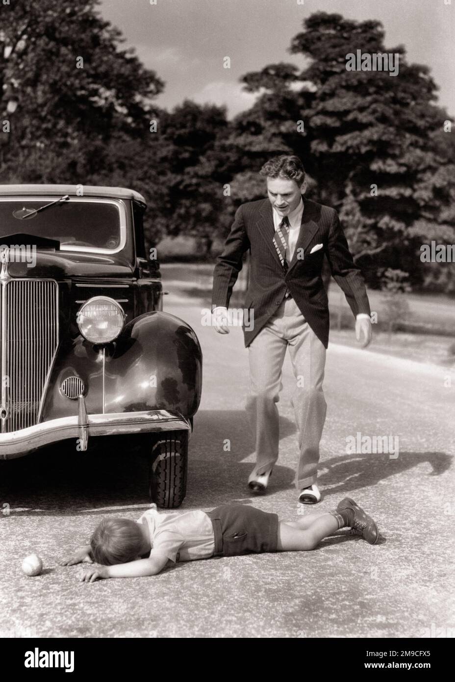 1930s 1940s BOY LYING PROSTRATE IN STREET HIT BY CAR CHASING BALL INTO ...