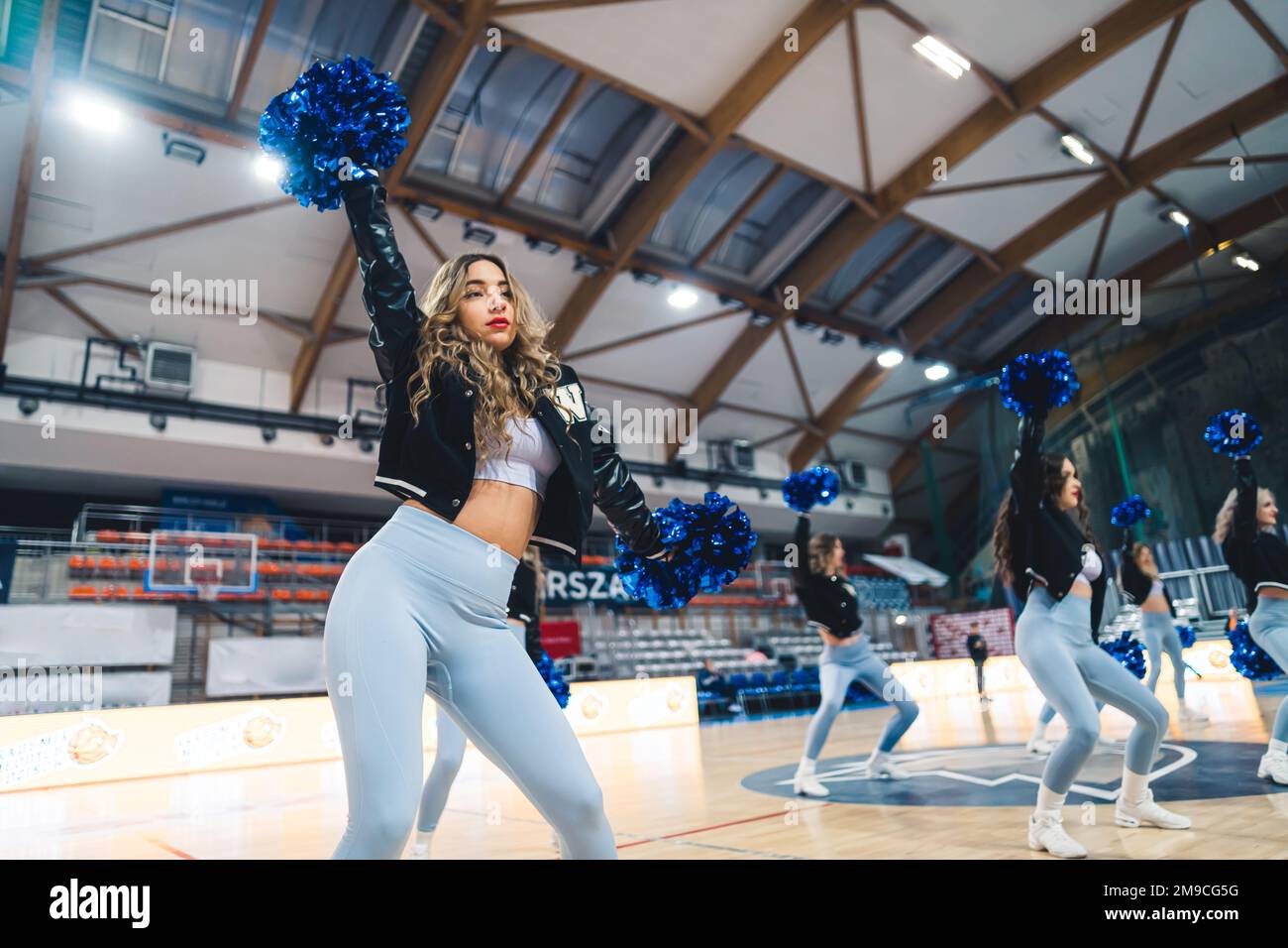 Medium shot of a cheerleader in a leather jacket with her arm stretched ...