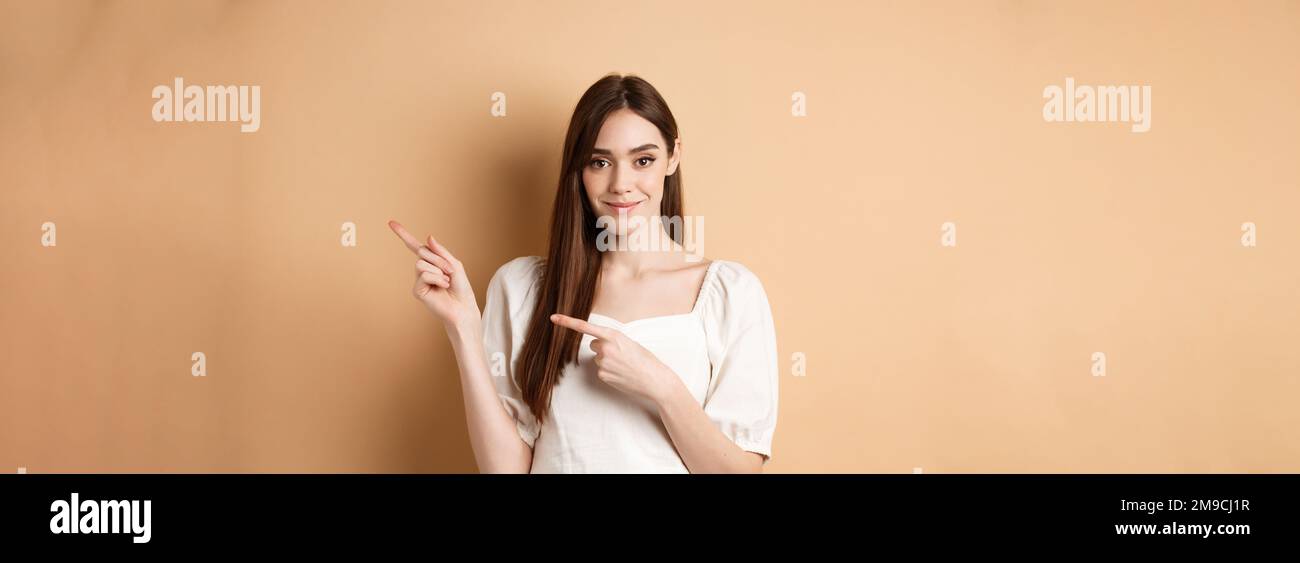 Beautiful young woman in dress pointing fingers right, showing logo and ...
