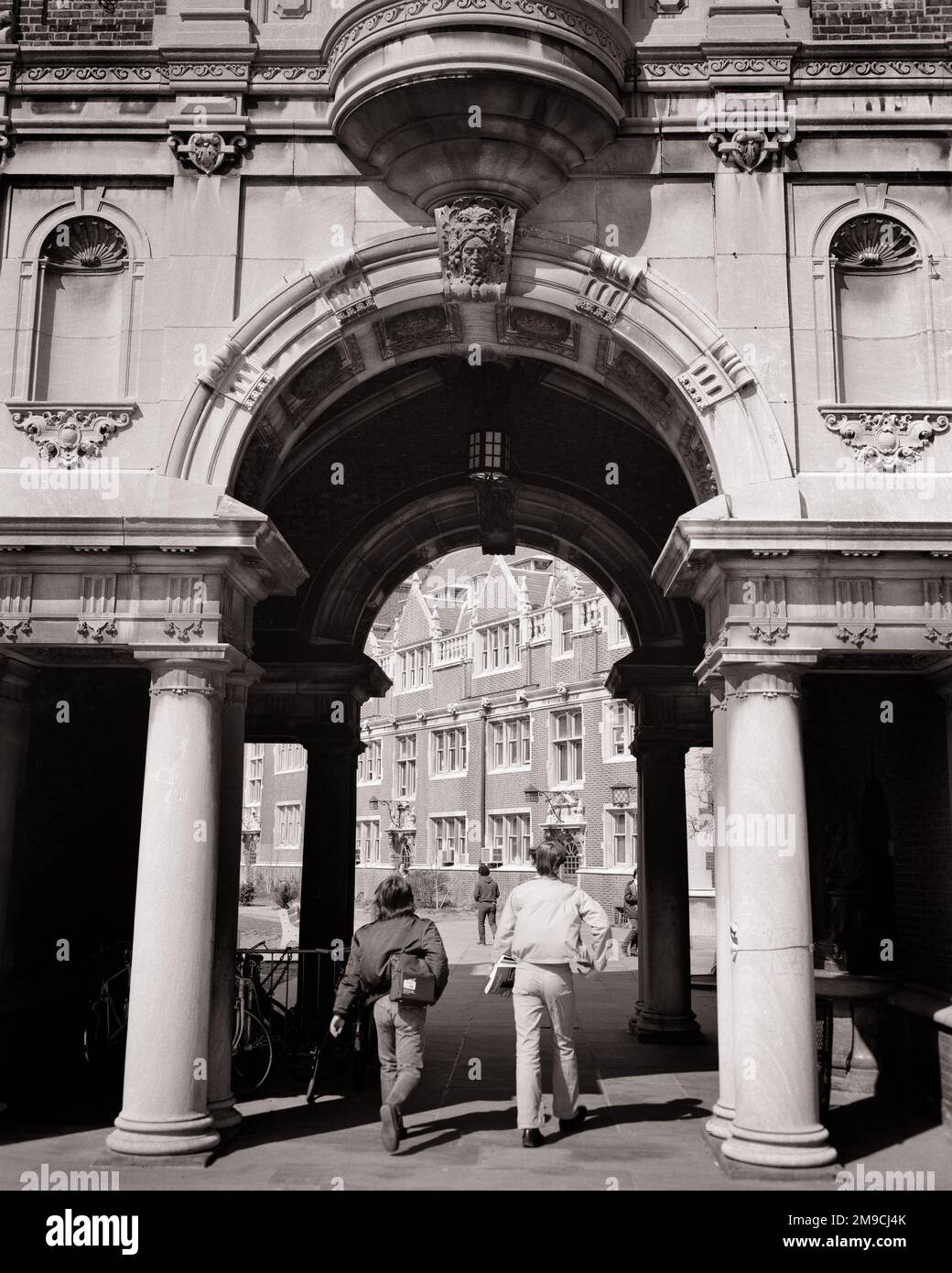1970s TWO ANONYMOUS MALE STUDENTS WALKING UNDER ORNATE ARCHITECTURAL ...