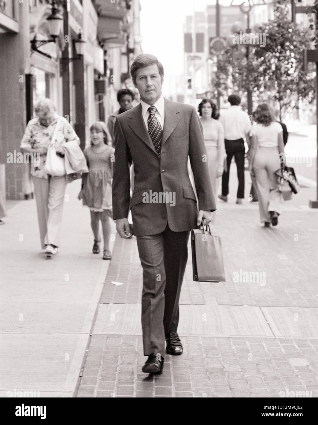 1970s SALESMAN WALKING DOWN CITY STREET LOOKING AT CAMERA WEARING SUIT ...