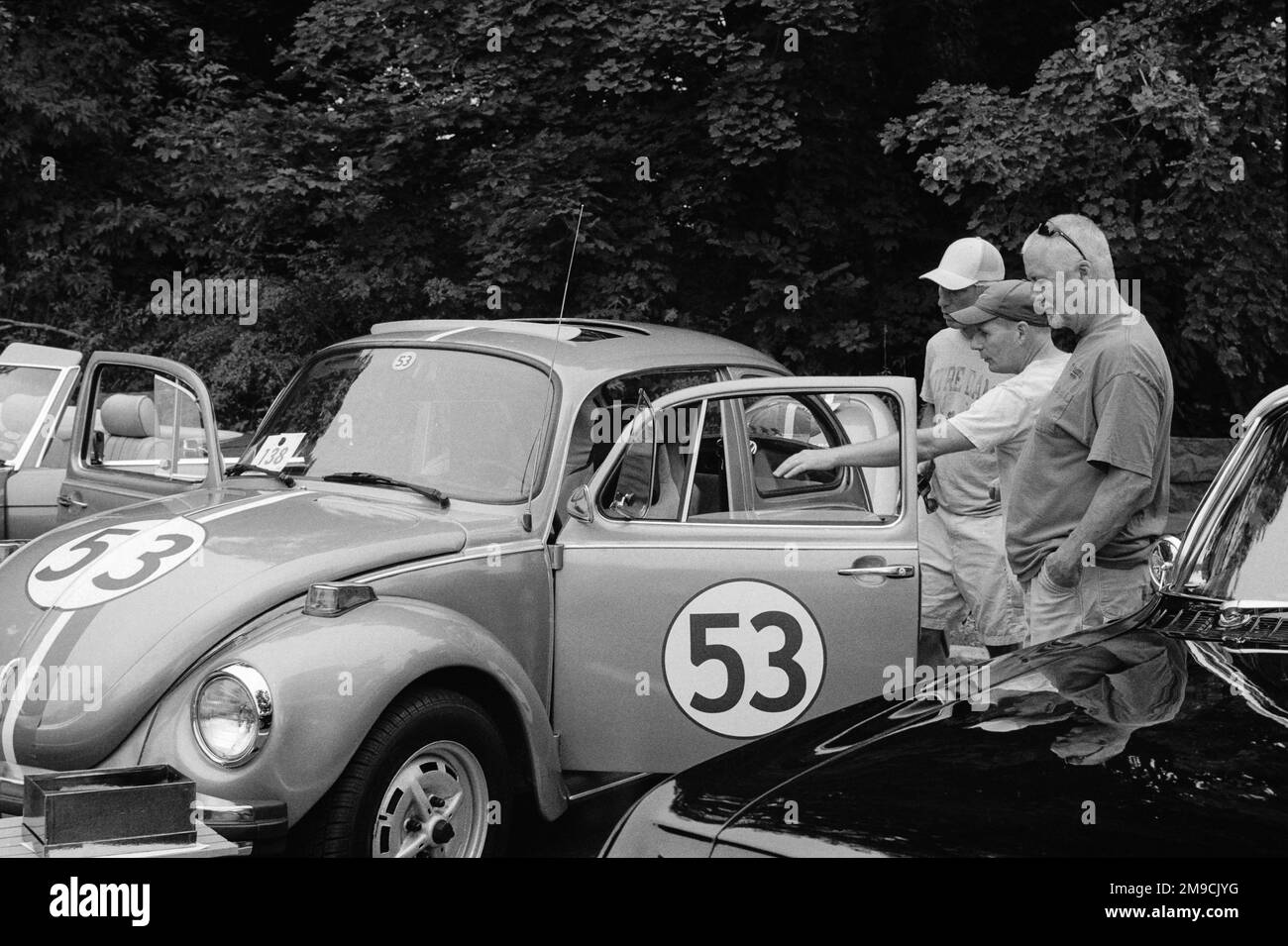 Three men inspecting a vintage Volkswagen beetle painted as Herbie the ...
