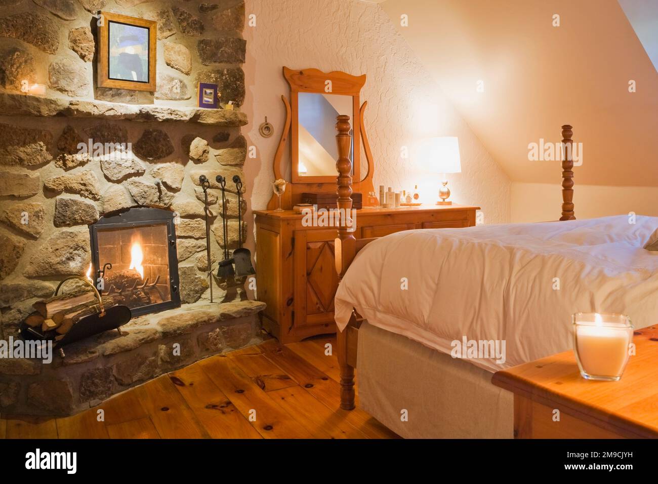 Lit fieldstone fireplace with wooden dresser and four poster queen size ...