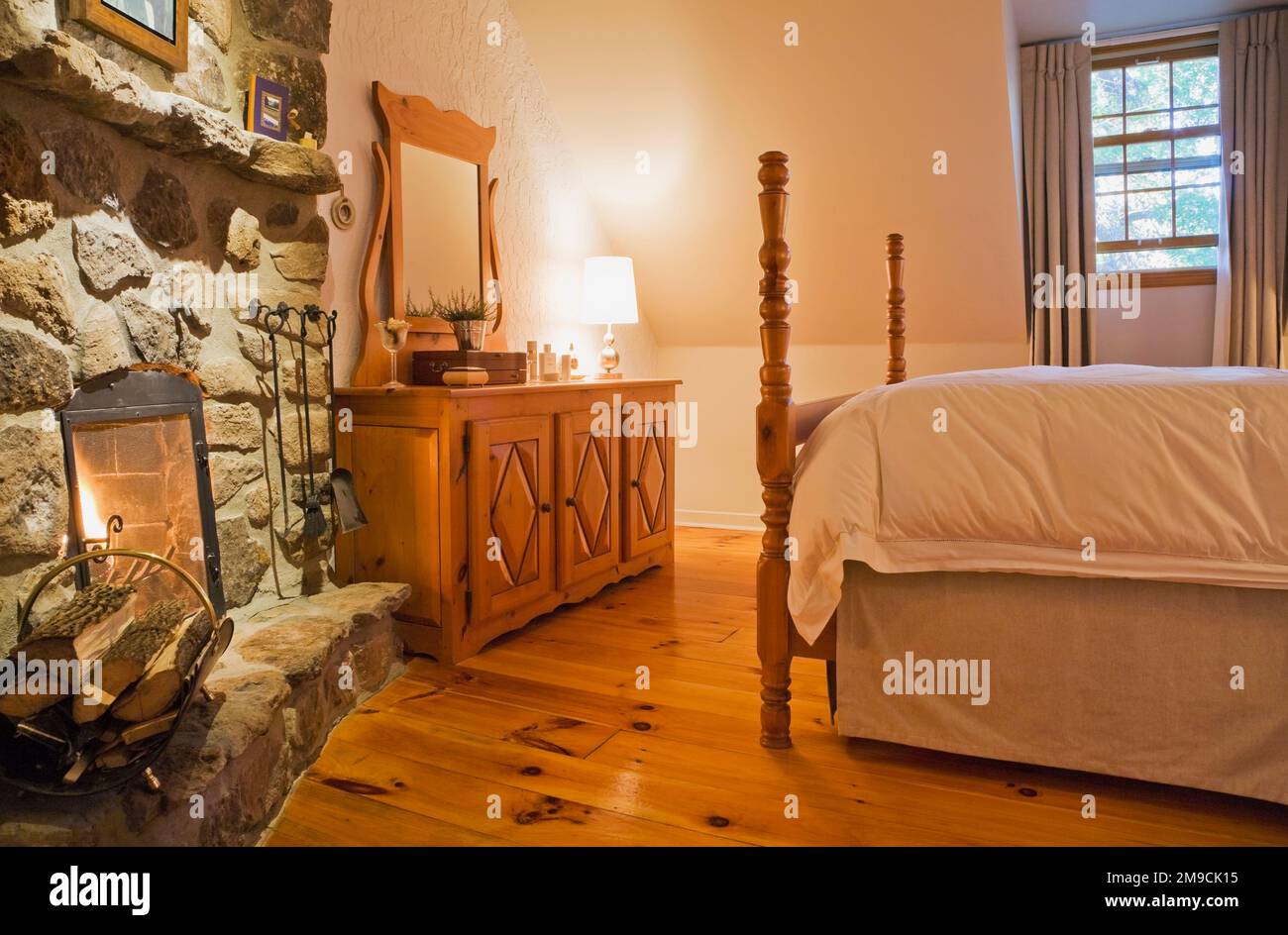 Lit fieldstone fireplace with wooden dresser and four poster queen size ...