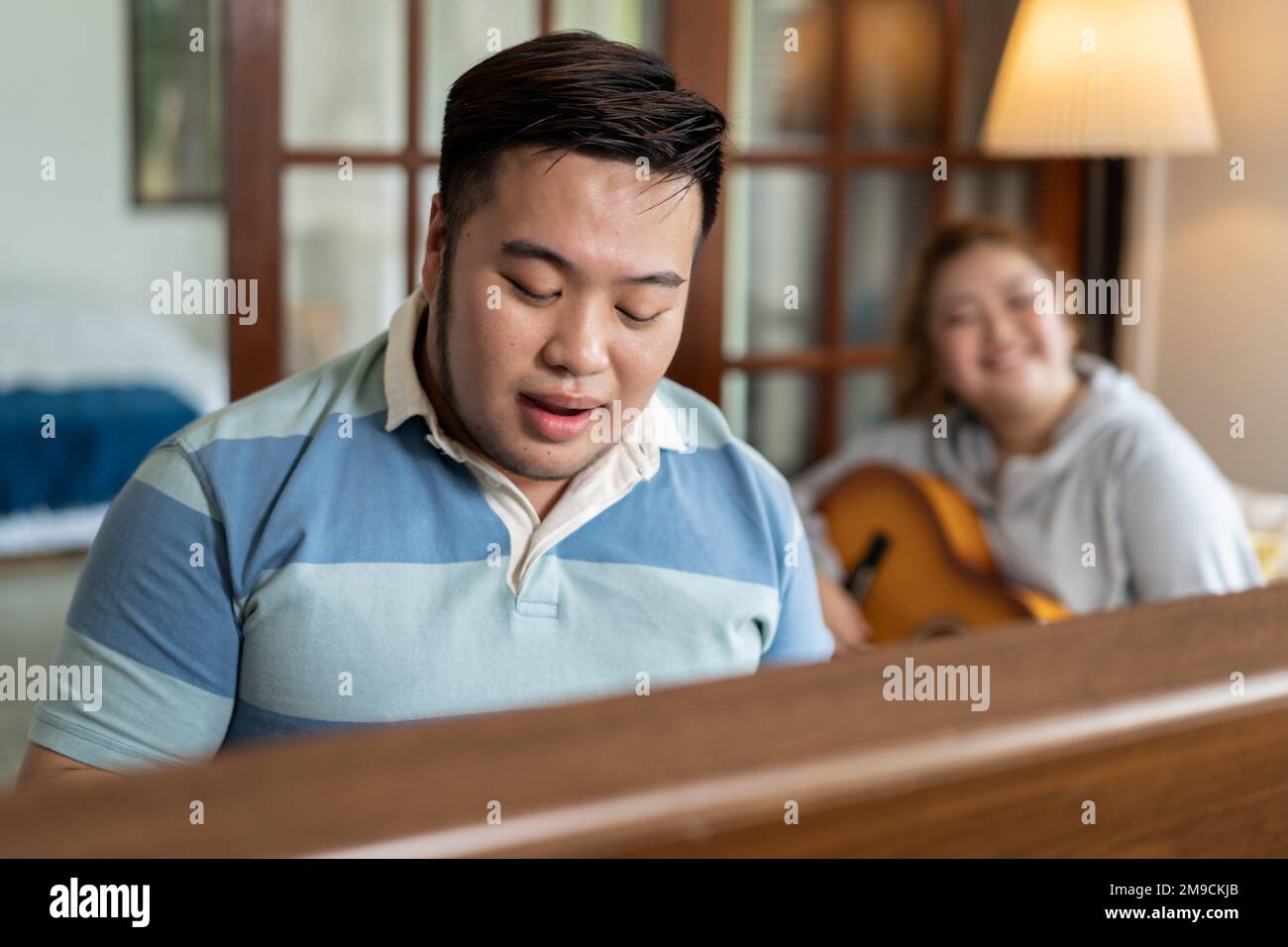 Young Asian chubby couple singing and playing acoustic guitar and piano ...