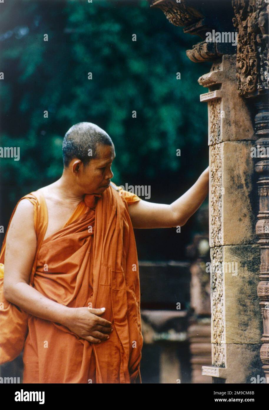 A reflective monk, pausing to rest against one of the columns at Angkor ...