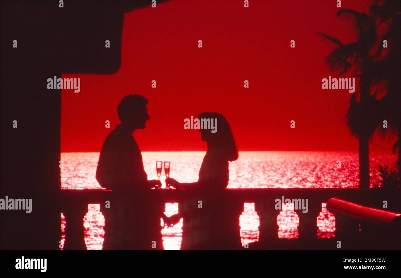 Silhouette of a couple at a balcony railing with champagne glasses ...