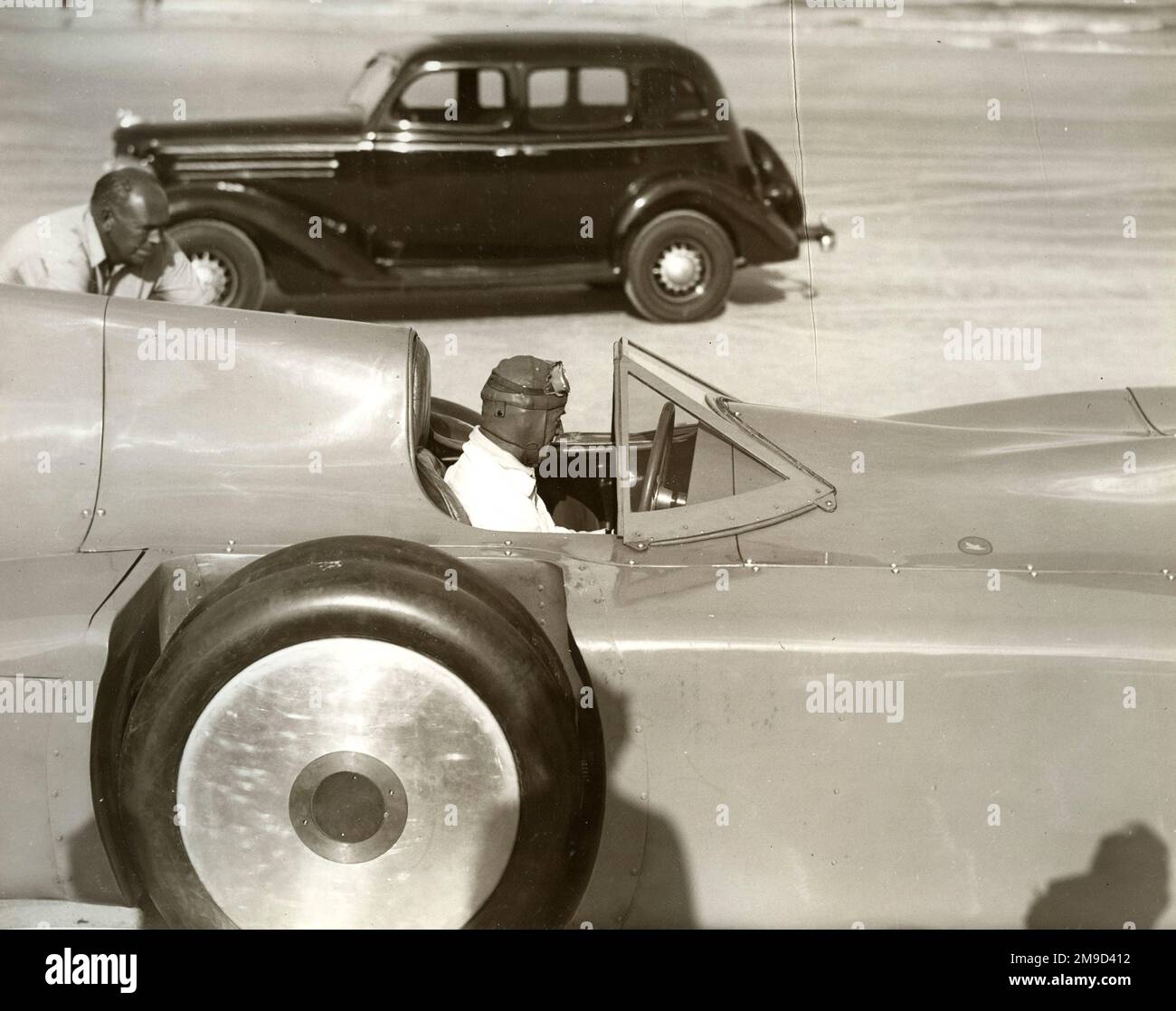 Side view of Campbell in Blue Bird with mechanic and car in background ...